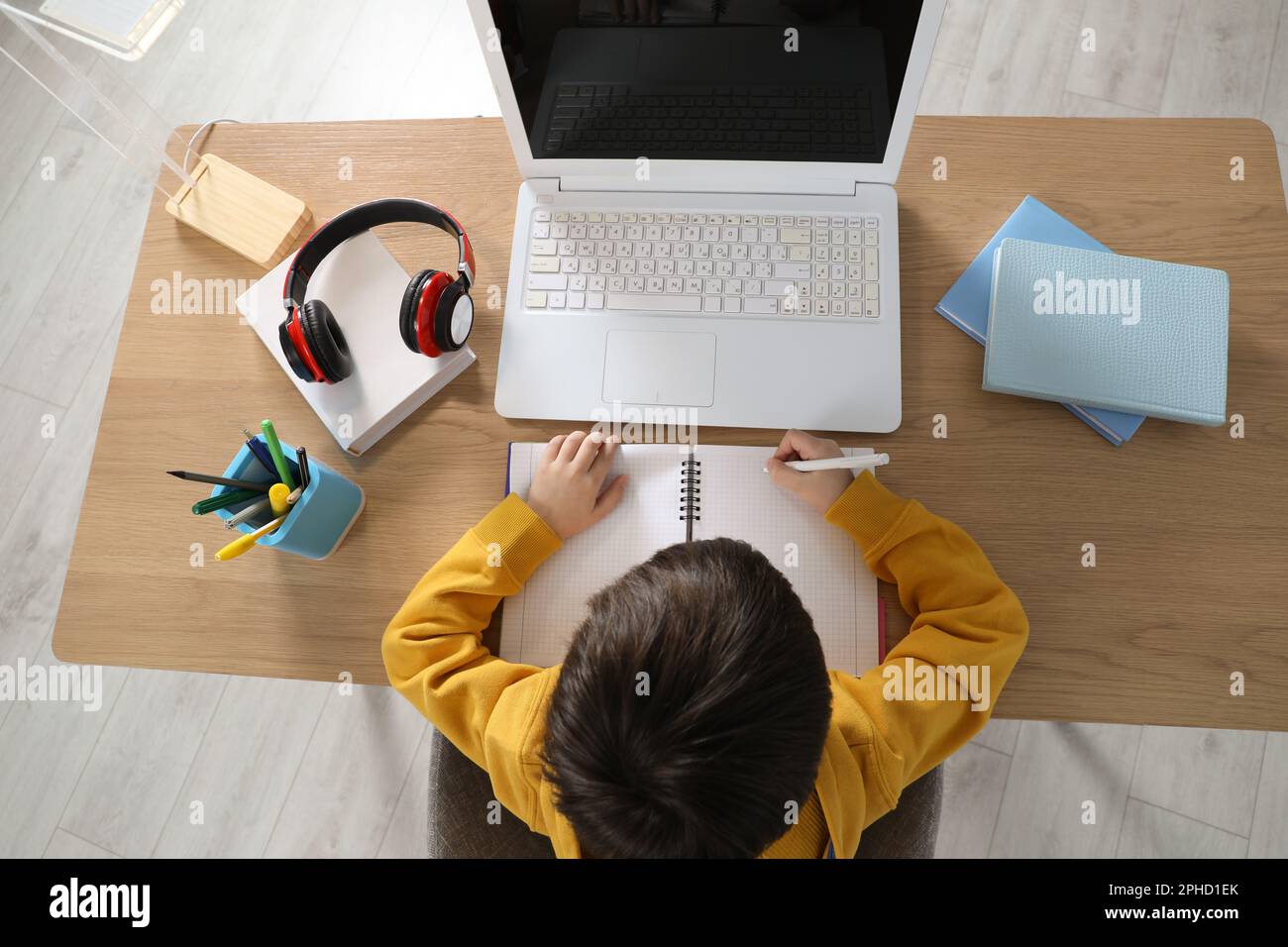 Cute little boy with modern laptop studying online at home, top view. E ...