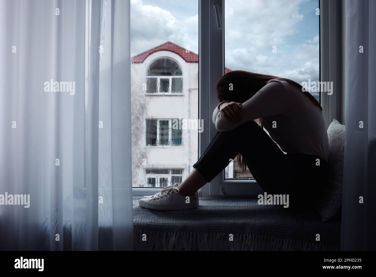 Unhappy young woman crying near window indoors, space for text ...