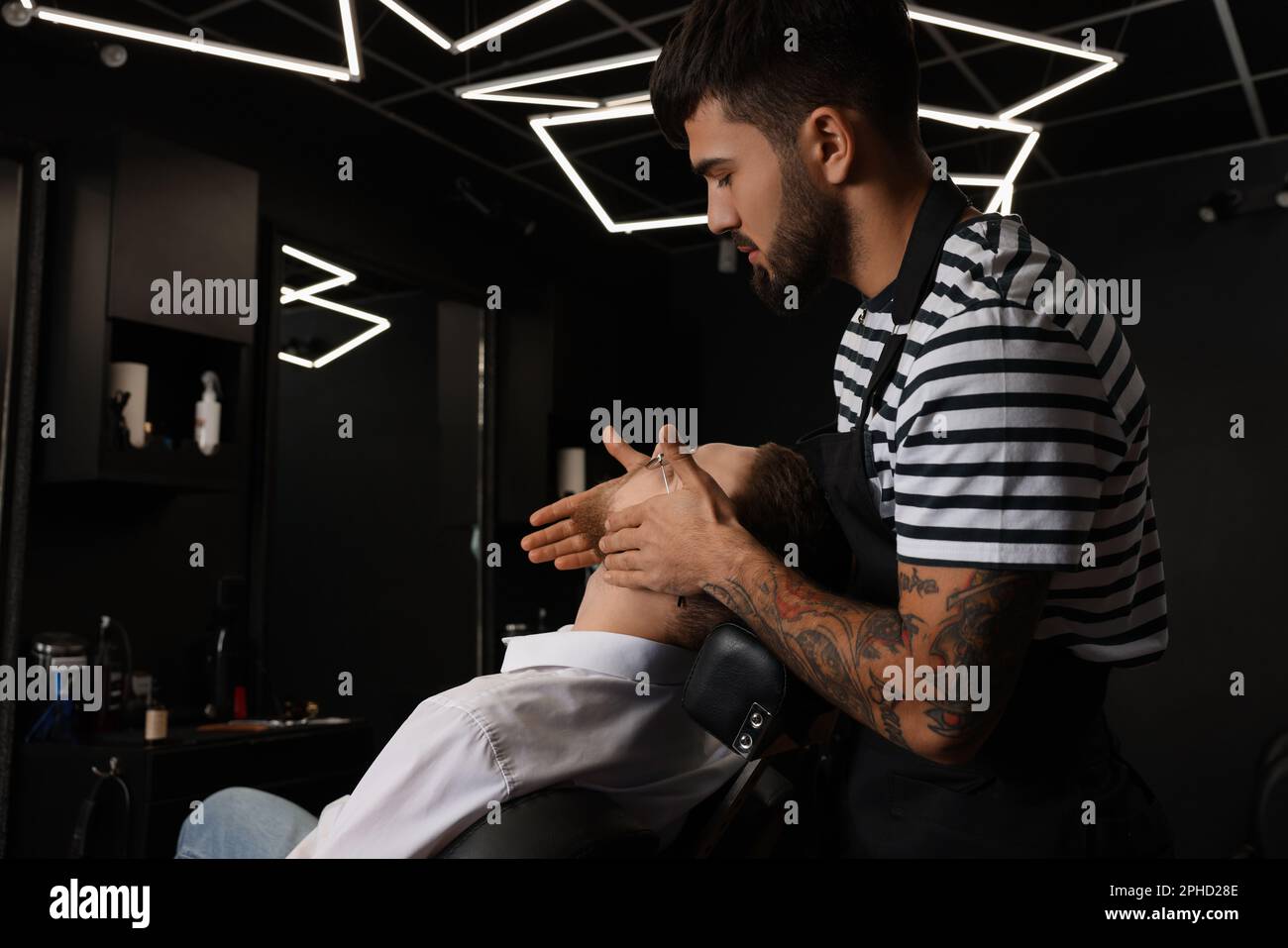 Hairdresser applying oil onto client's beard in barbershop. Professional shaving service Stock ...