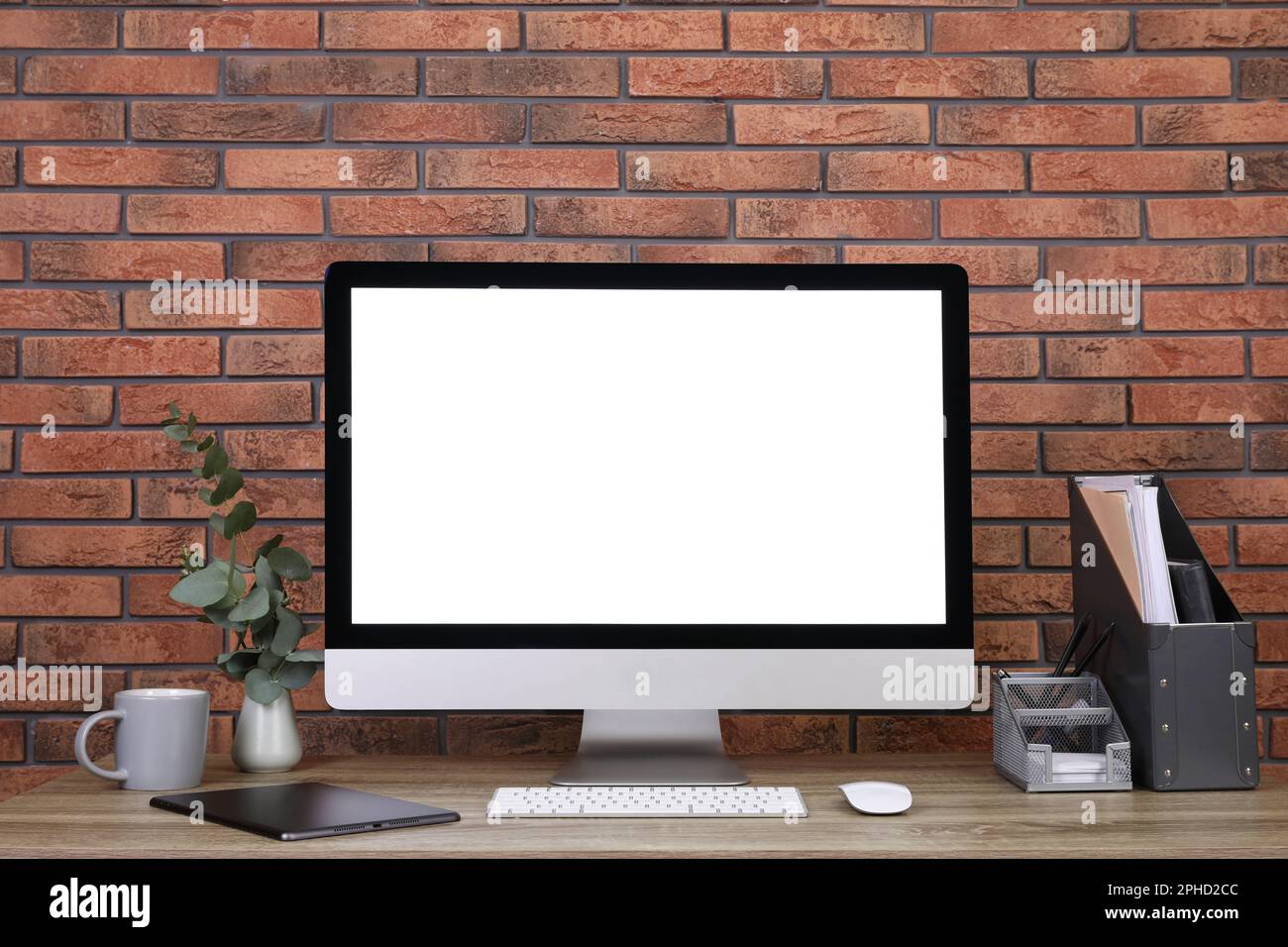 Modern computer with blank screen on desk near brick wall, space for ...