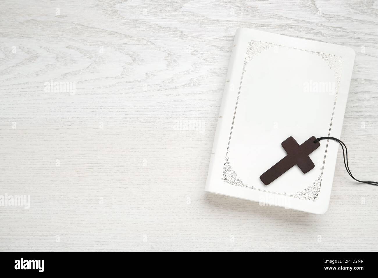 Wooden Christian cross and Bible on white table, top view. Space for ...