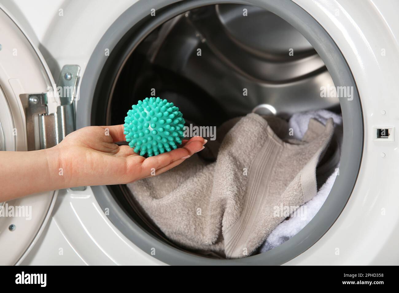 Woman putting green dryer ball into washing machine, closeup Stock ...