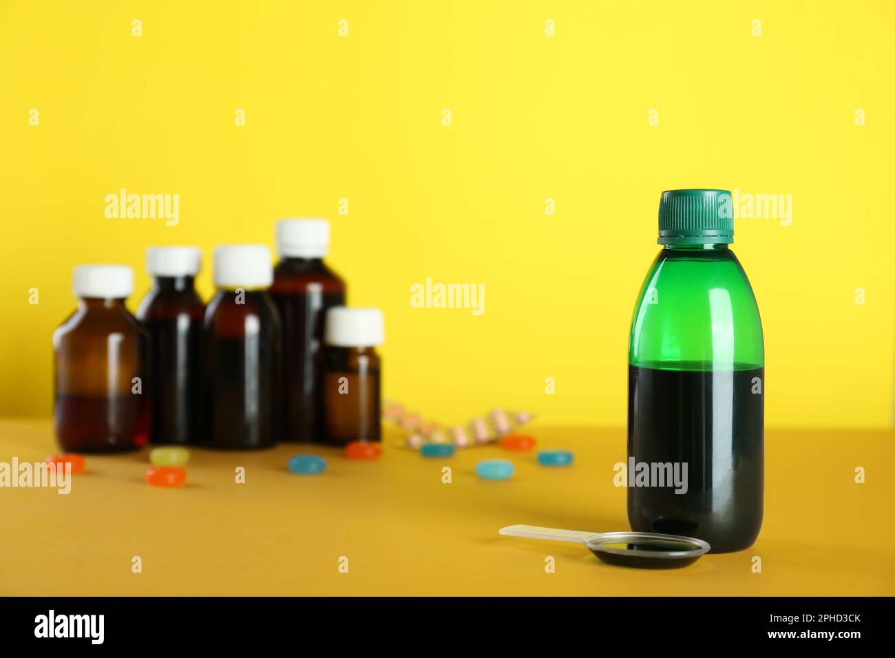 Bottle of cough syrup and dosing spoon on yellow background. Space for ...