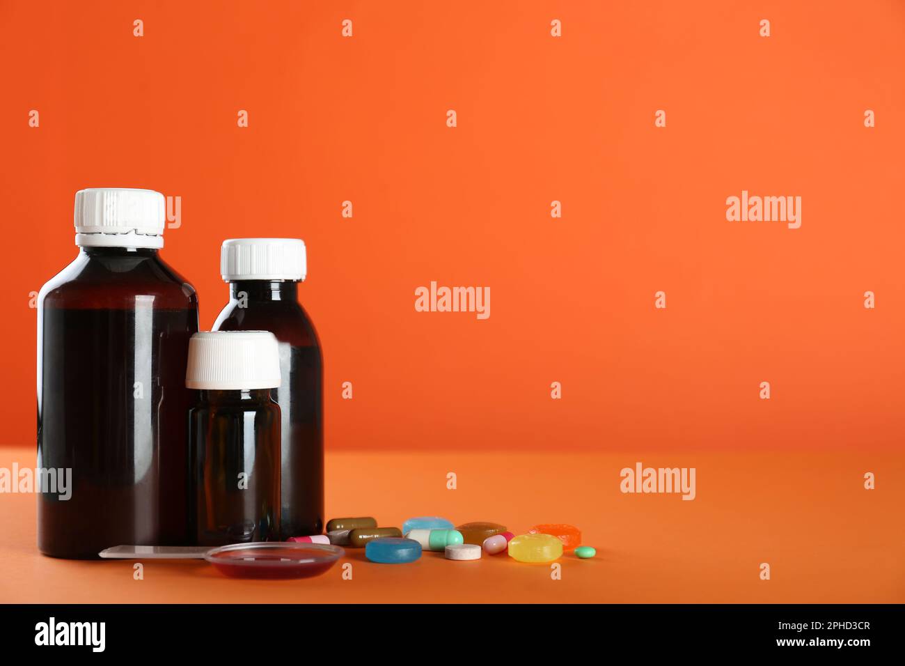 Bottles of cough syrup, dosing spoon and pills on orange background ...