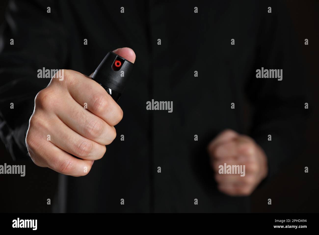 Man using pepper spray on black background, closeup. Space for text ...