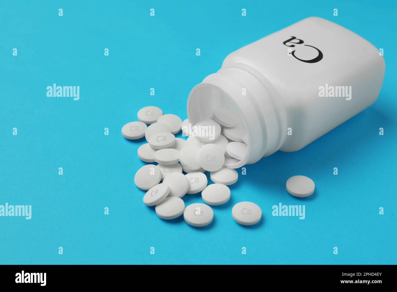 Overturned bottle of calcium supplement pills on light blue background ...