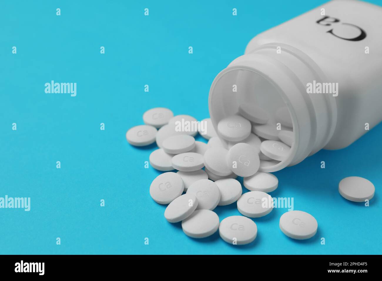 Overturned bottle of calcium supplement pills on light blue background ...