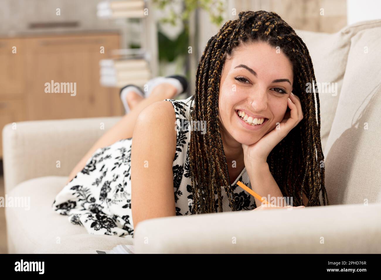 Young student lying face down on her home sofa studying, pencil visible ...