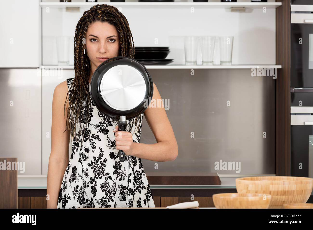 Young woman poses as a warrior armed with a frying pan in the kitchen ...