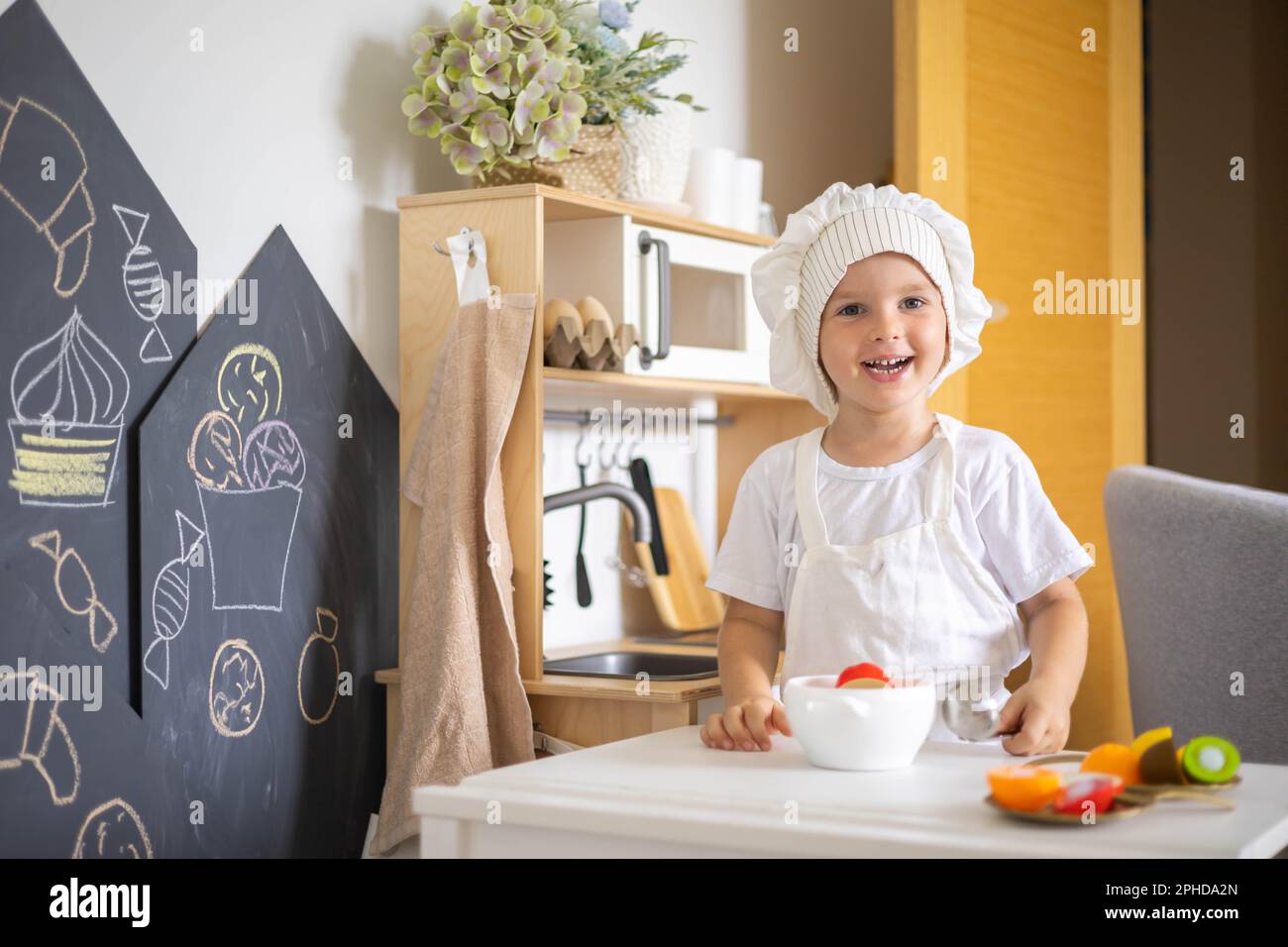 Cute male kid preparing toy food boiling vegetables on cooker at ...