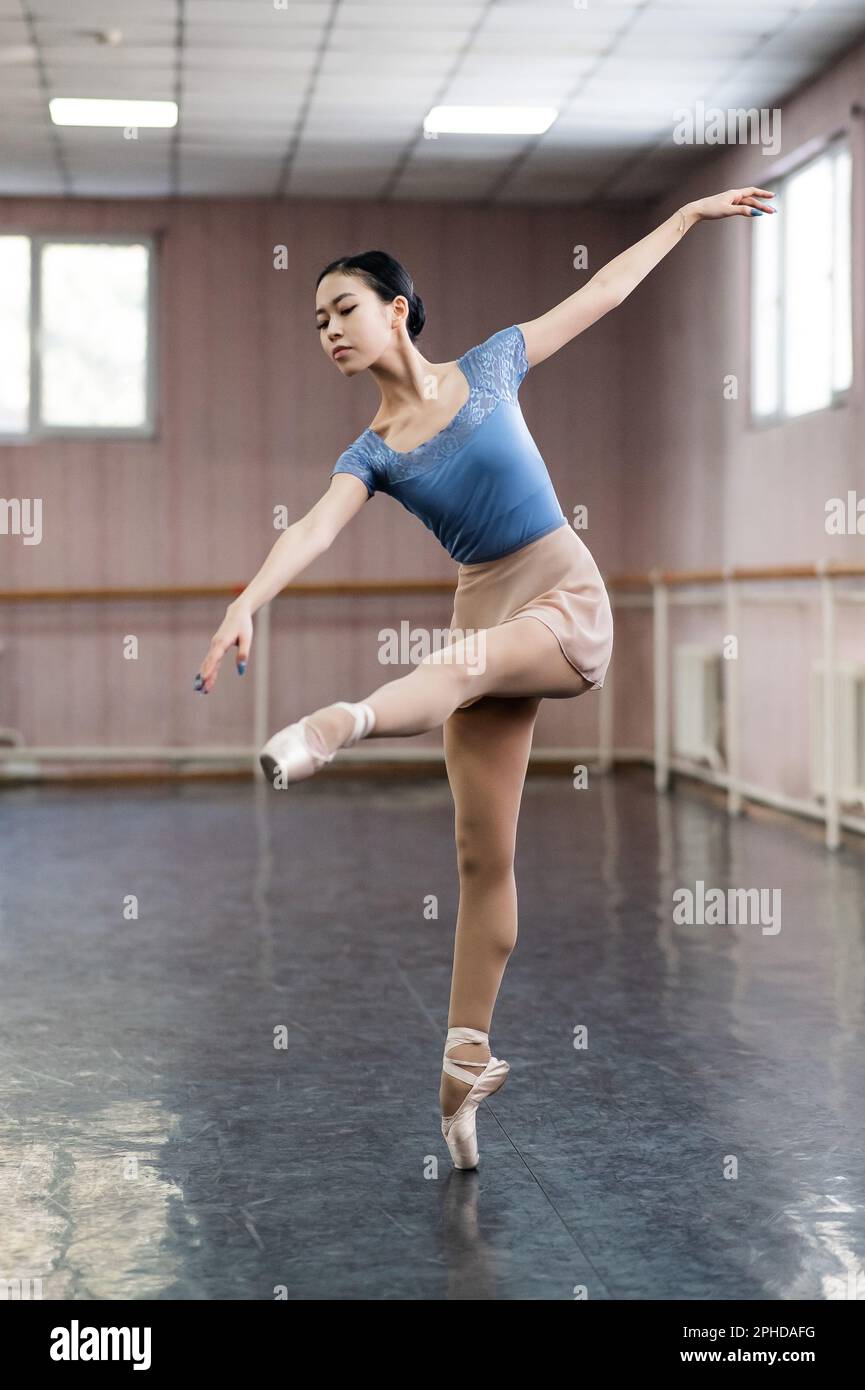 Graceful Asian ballerina in a blue bodysuit and a beige skirt is ...