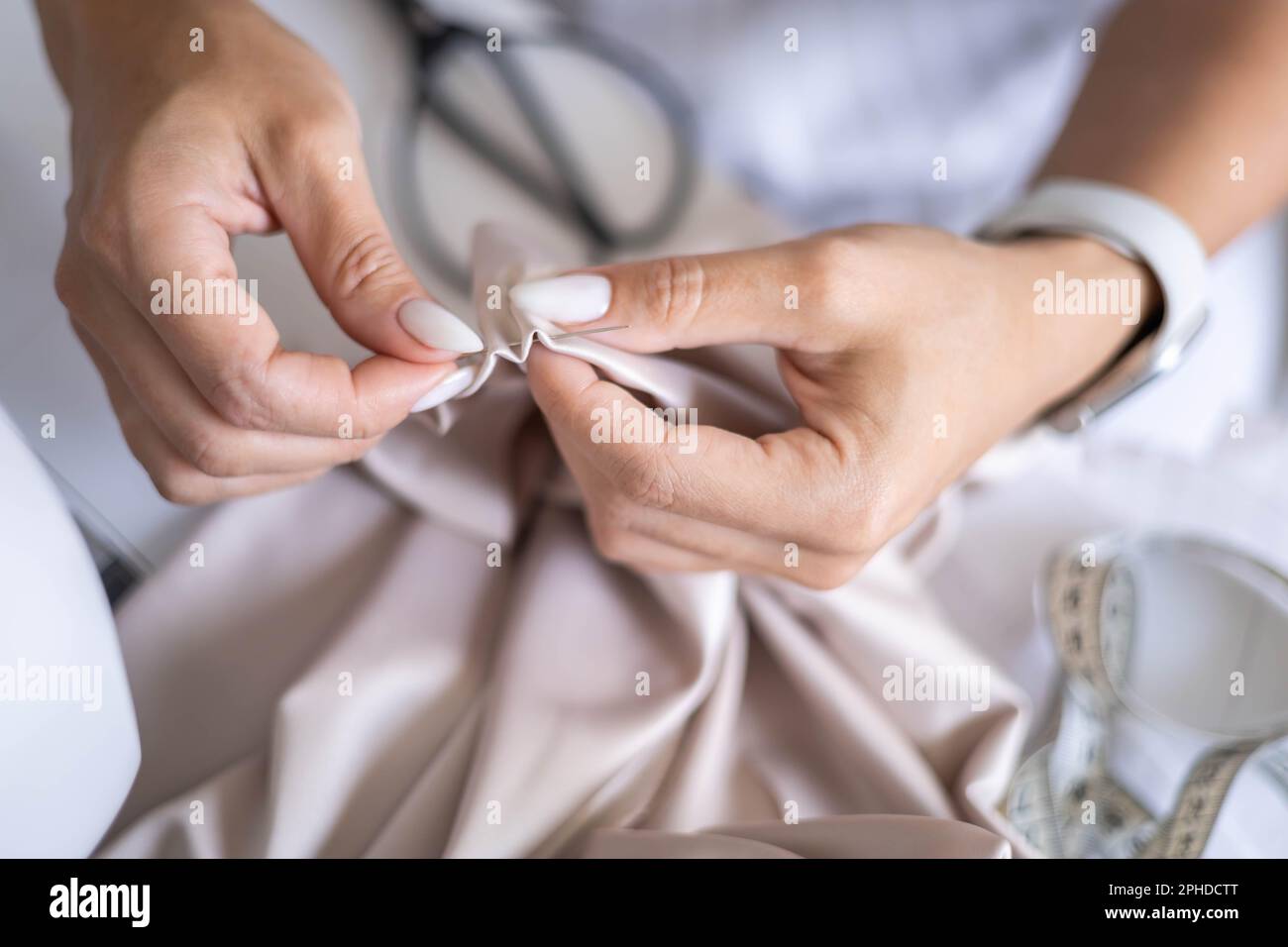 Female tailor hands sewing beige textile with needle and thread process ...