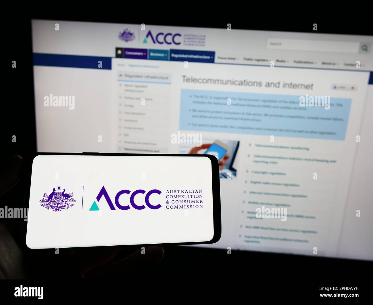 Person holding mobile phone with logo of Australian Competition and ...