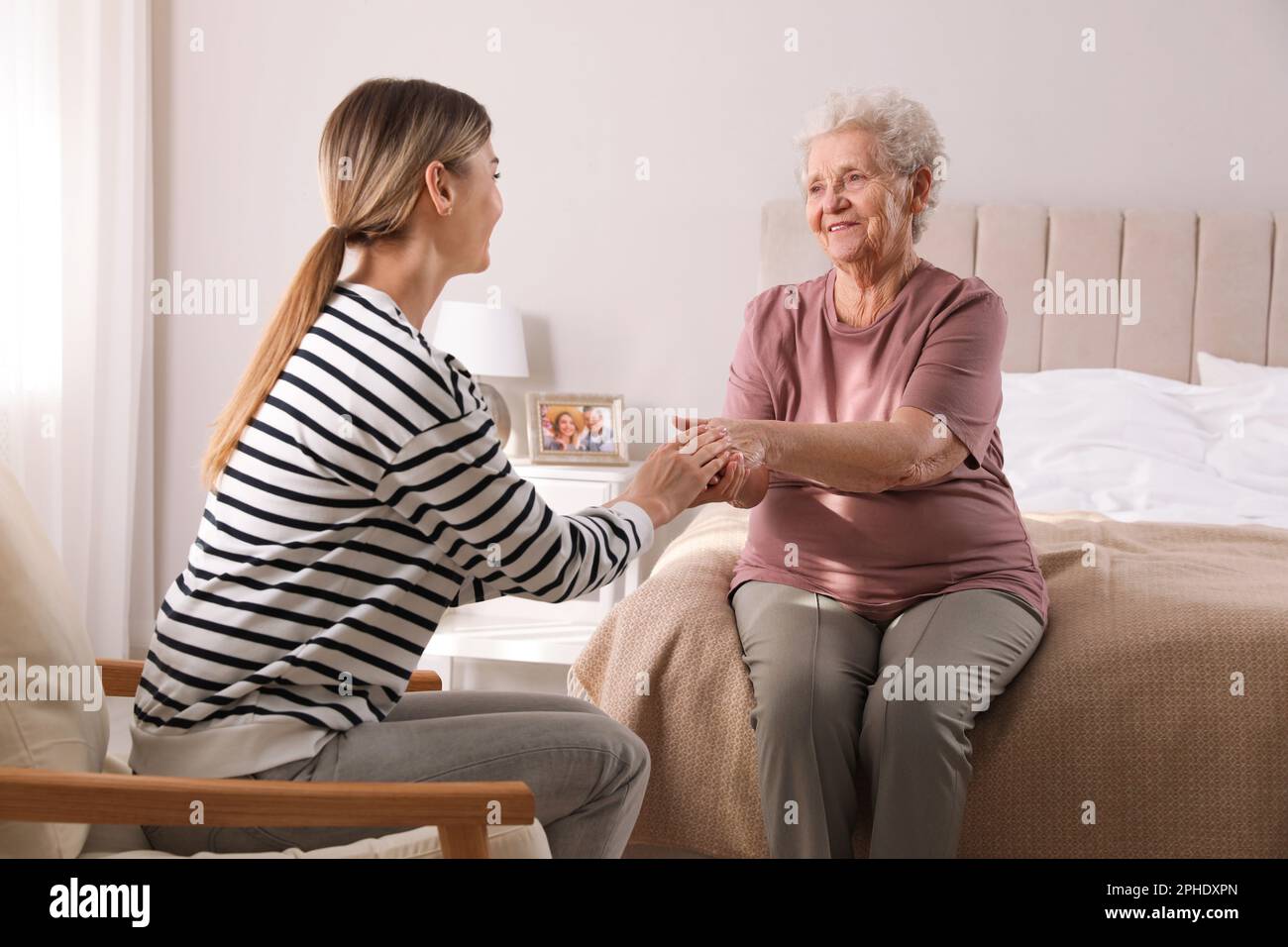 Young caregiver talking to senior woman in bedroom. Home care service ...