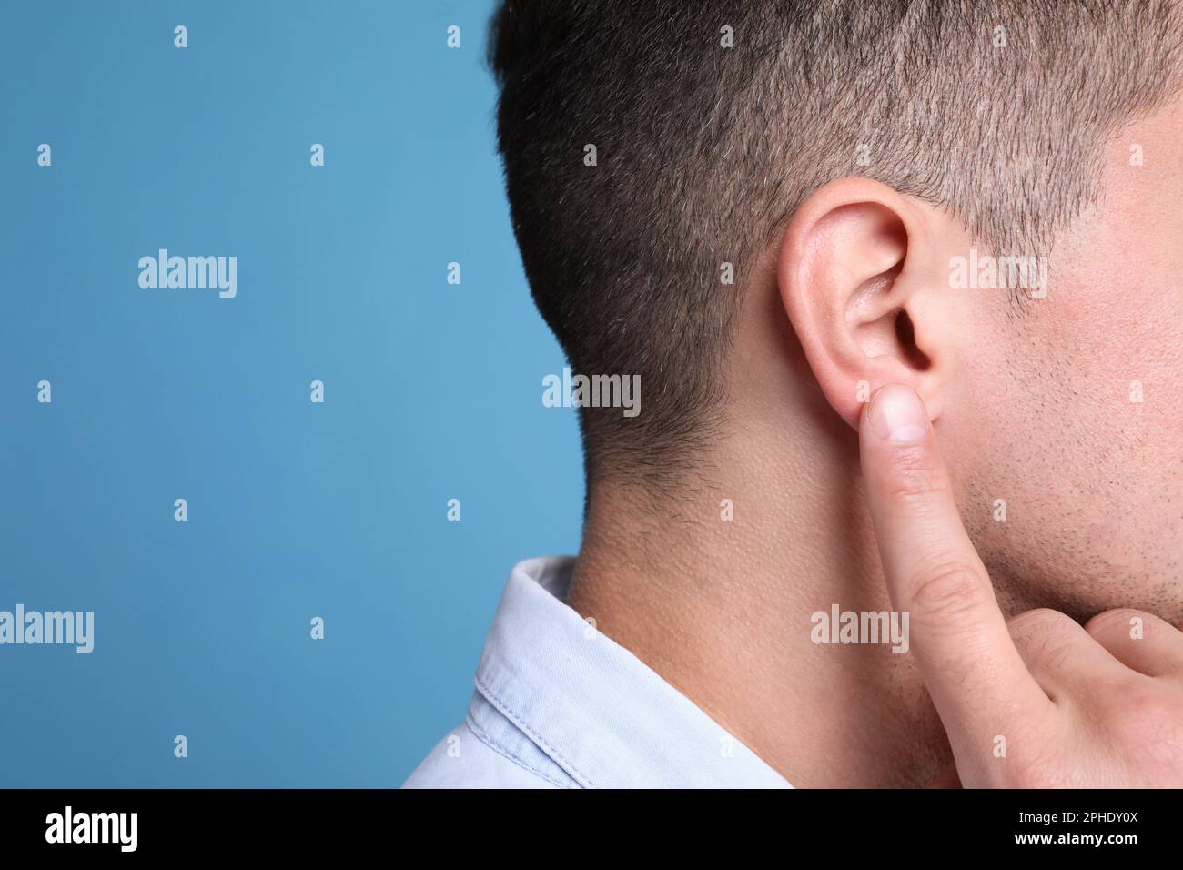 Man pointing at his ear on light blue background, closeup. Space for ...