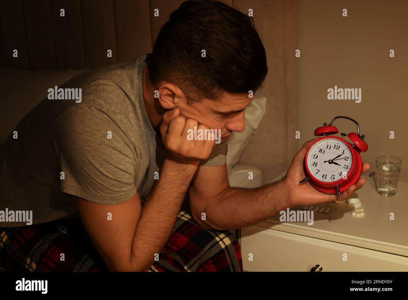 Man suffering from insomnia looking at time on alarm clock in bedroom ...