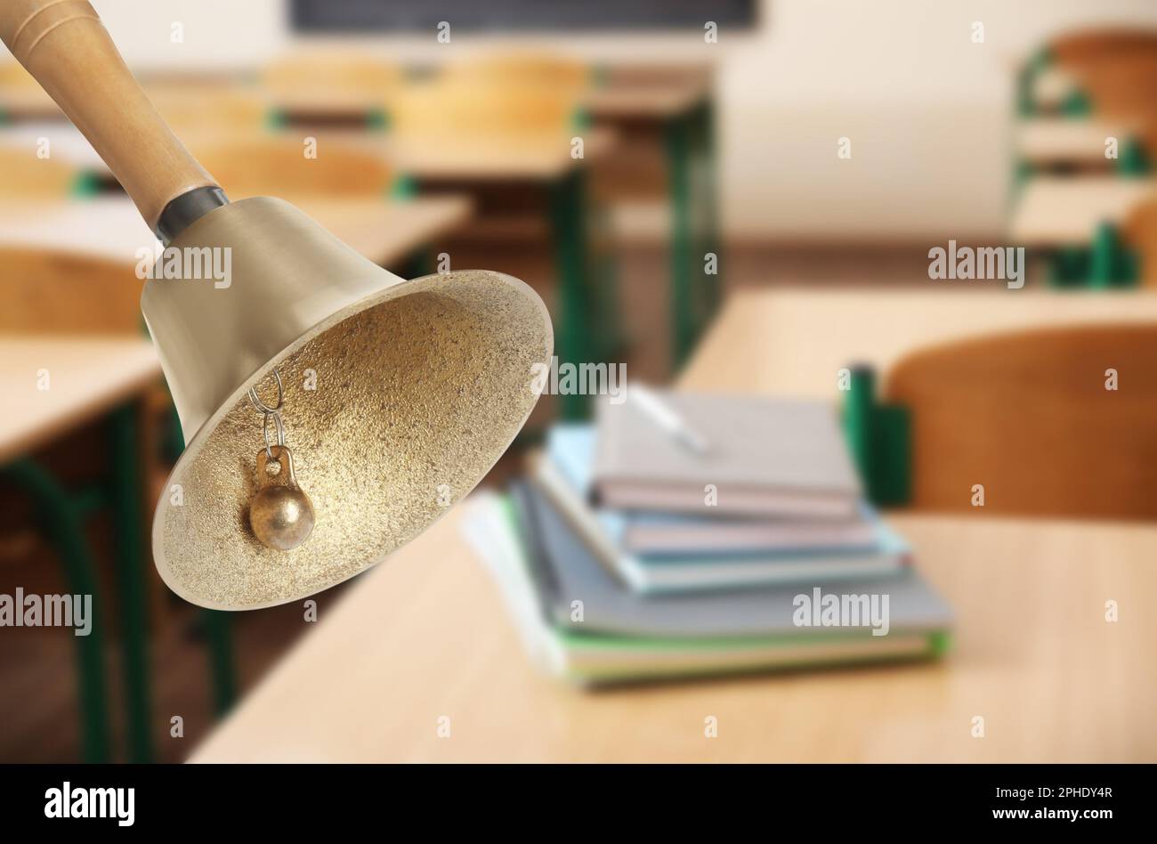 Golden school bell with wooden handle and blurred view of books on desk ...