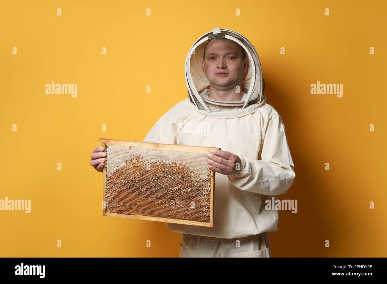 Beekeeper in uniform holding hive frame with honeycomb on yellow ...