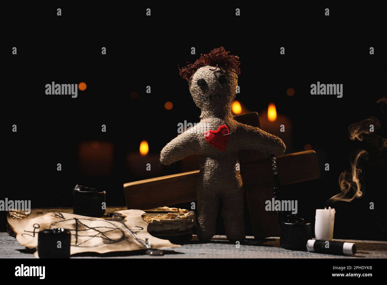 Voodoo doll with pin in heart and ceremonial items on wooden table ...