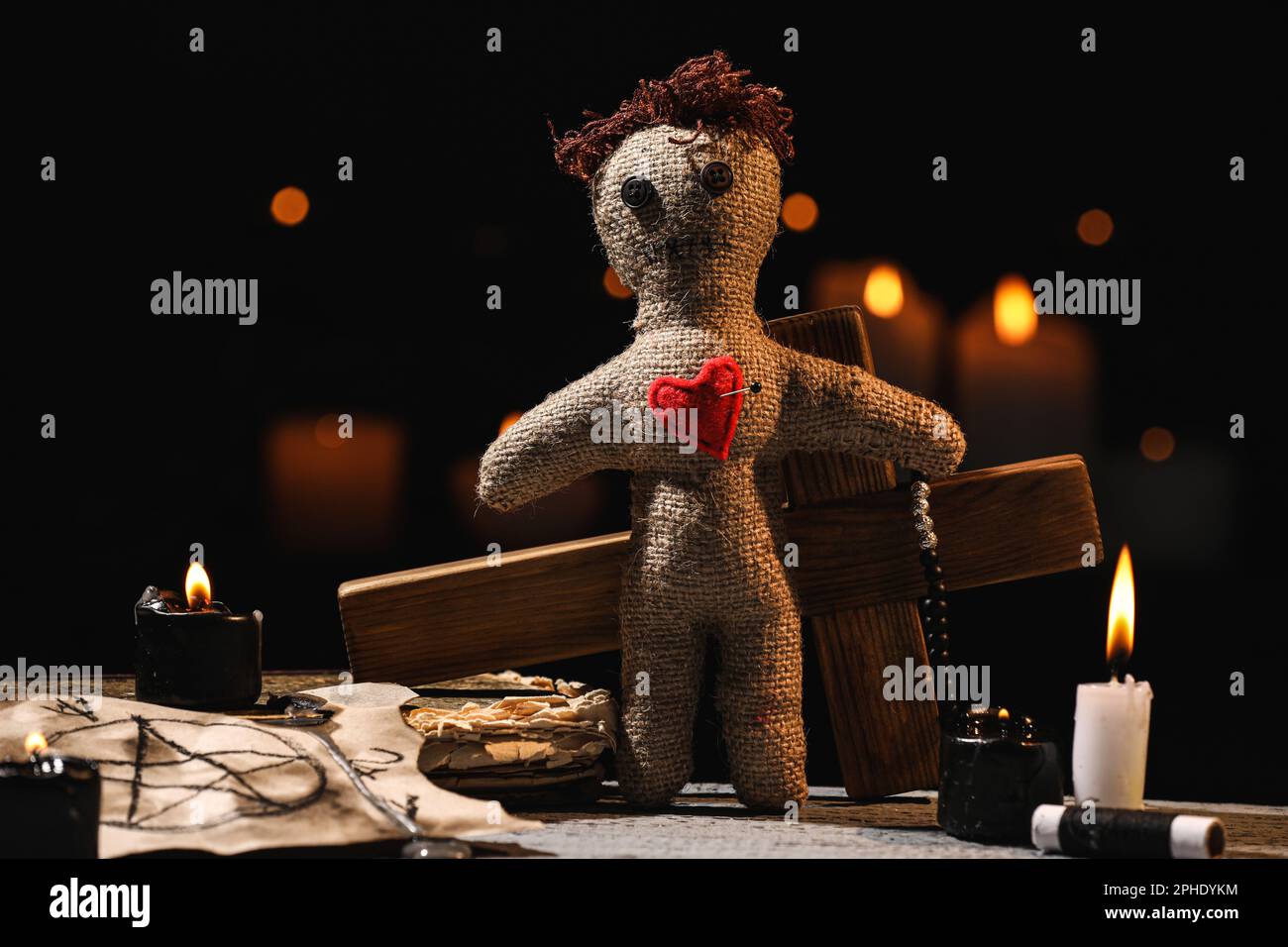 Voodoo doll with pin in heart and ceremonial items on wooden table ...