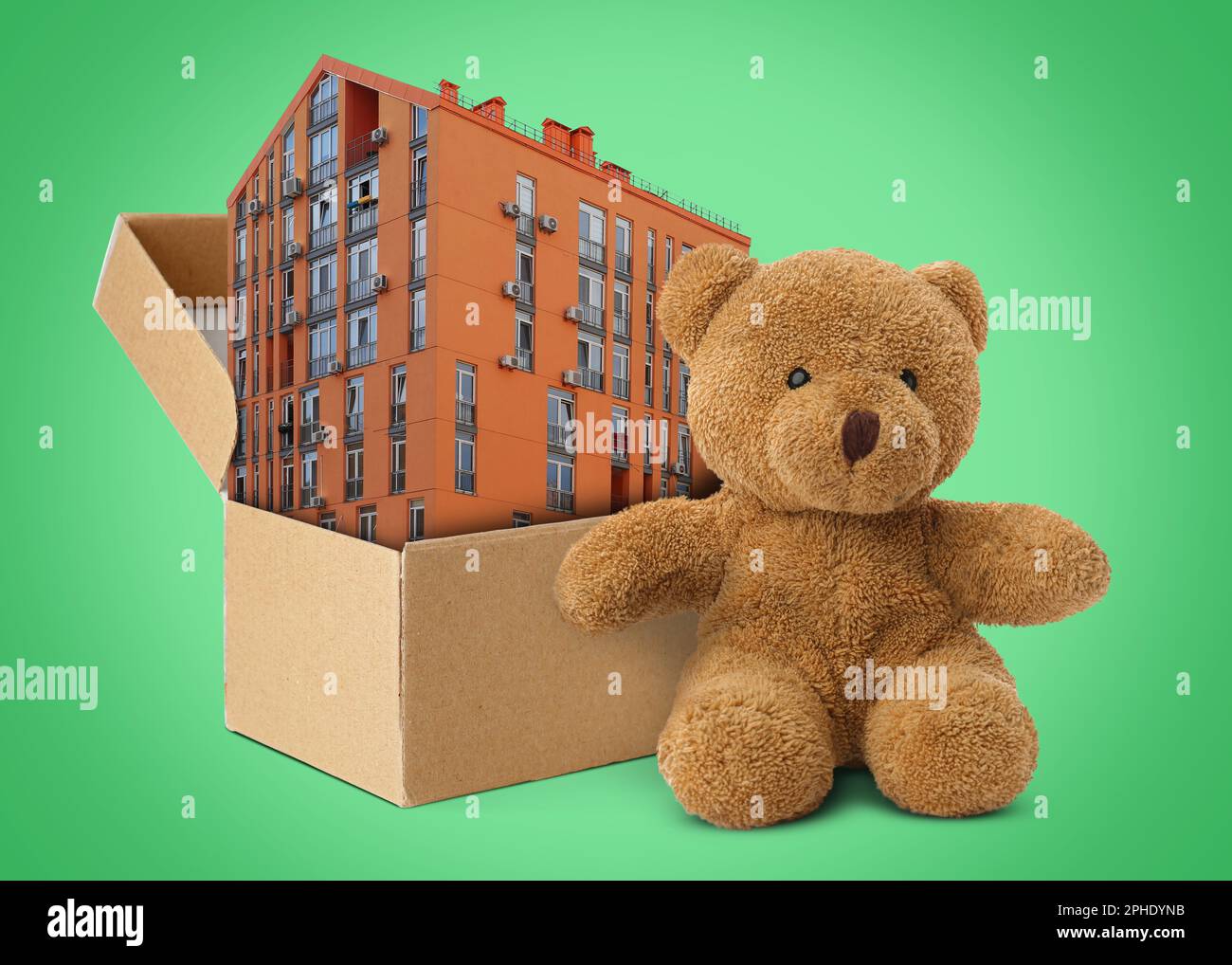 Cute toy bear near cardboard box with building on green background ...