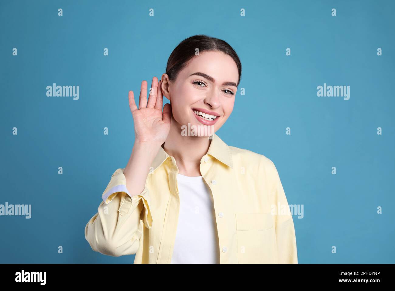 Young woman showing hand to ear gesture on light blue background Stock ...