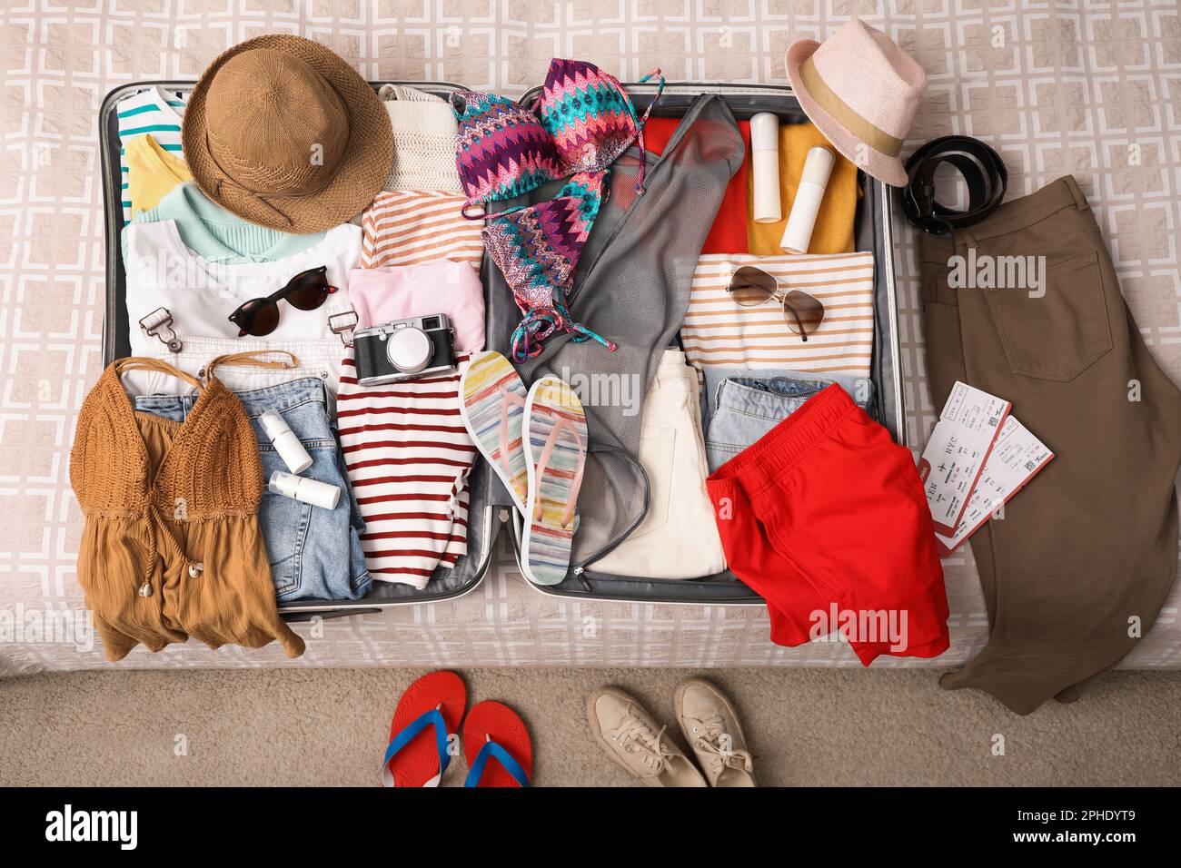 Open suitcase with clothes and accessories on bed indoors, top view ...