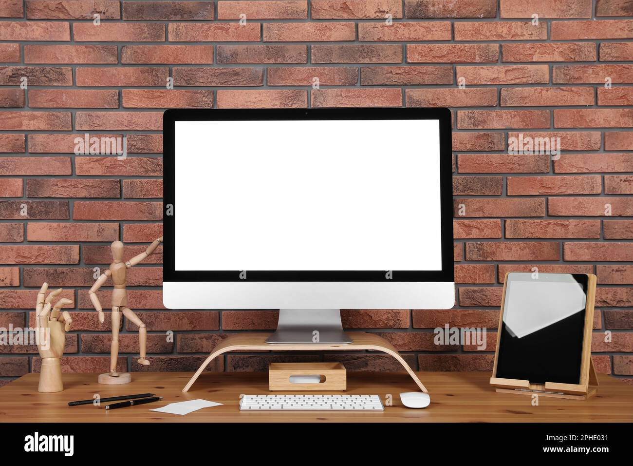 Modern computer and tablet with blank screens on desk near brick wall ...