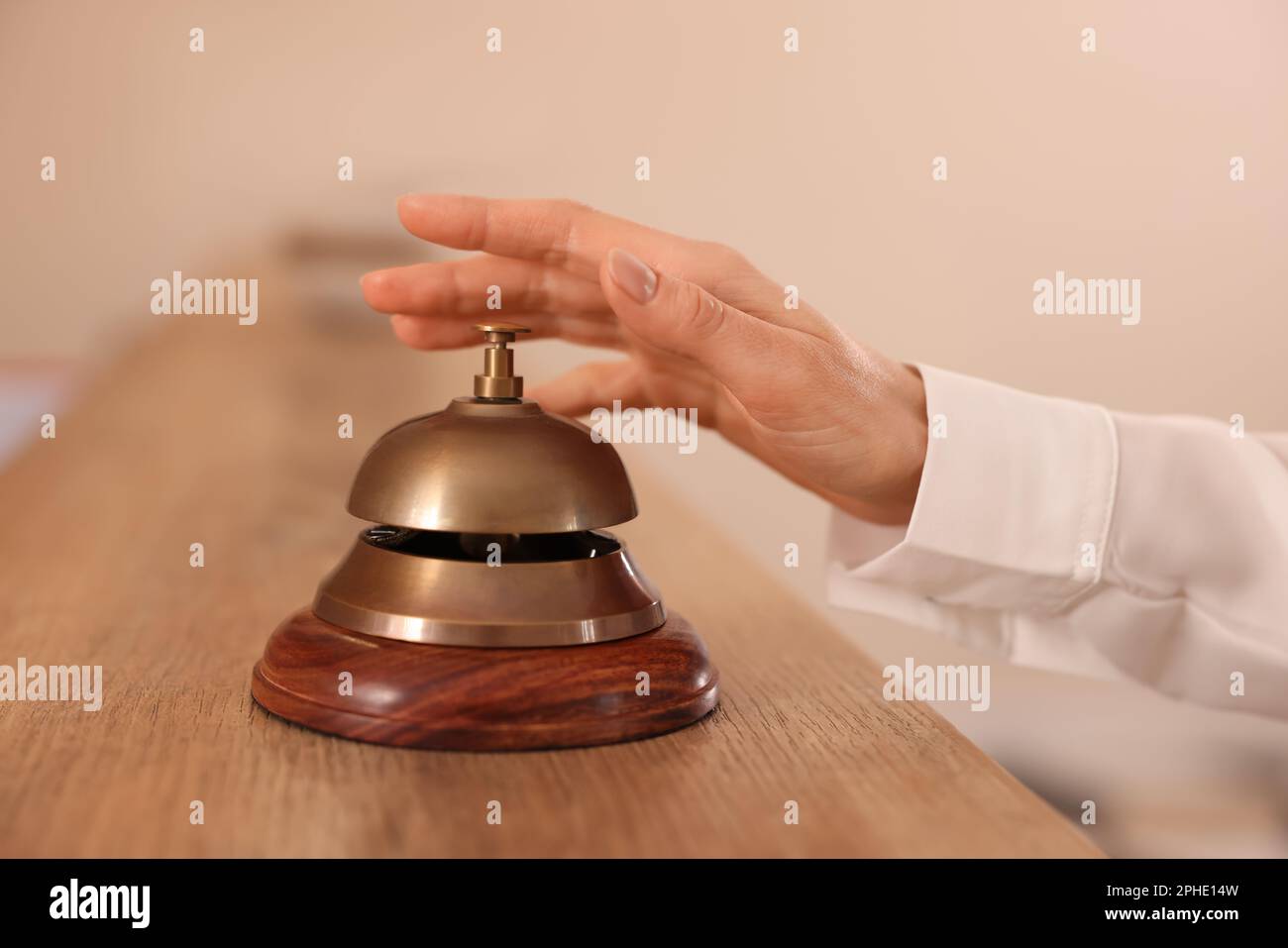 Woman ringing hotel service bell at wooden reception desk, closeup ...