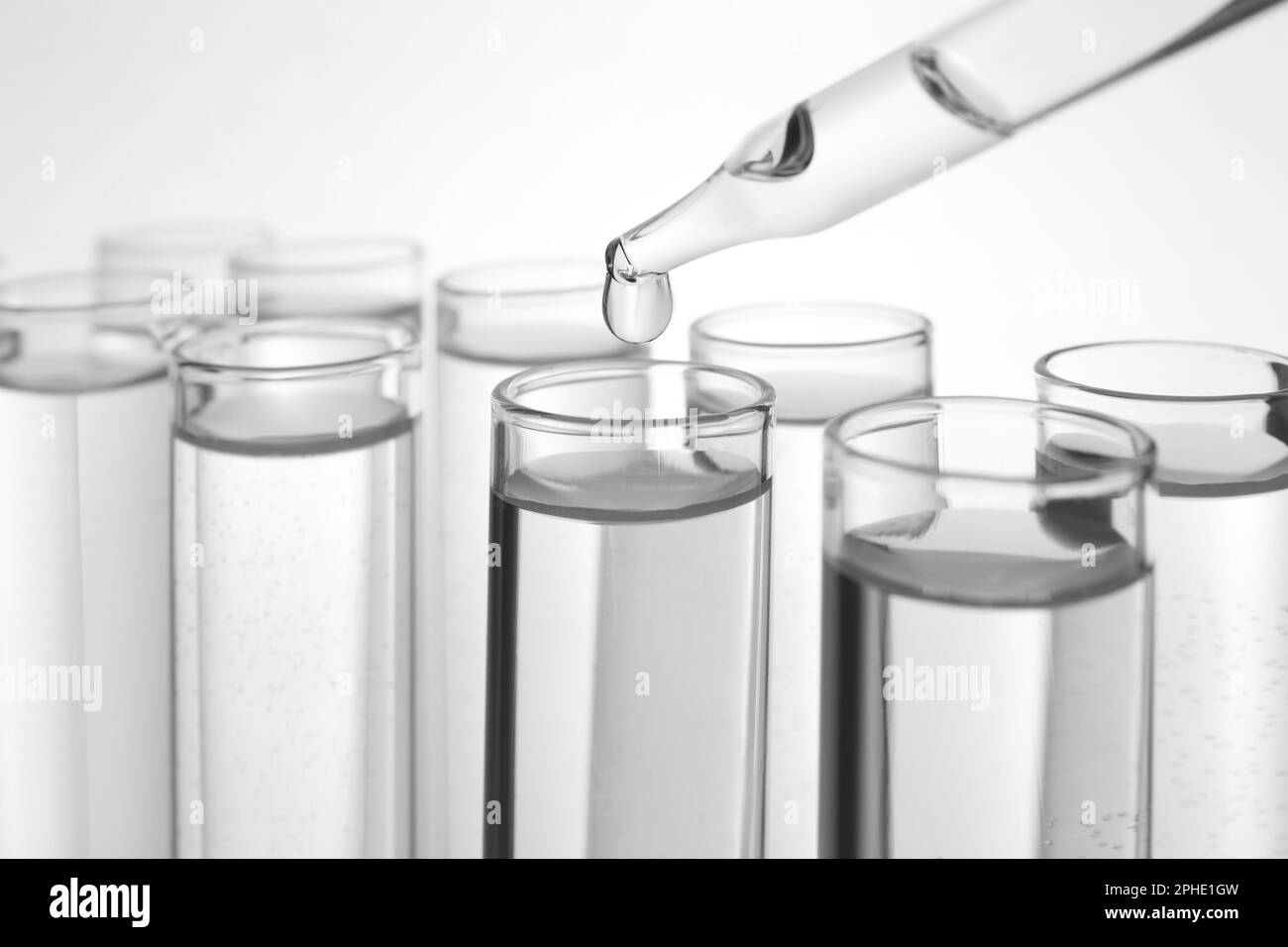 Dripping transparent liquid into test tube on white background, closeup ...