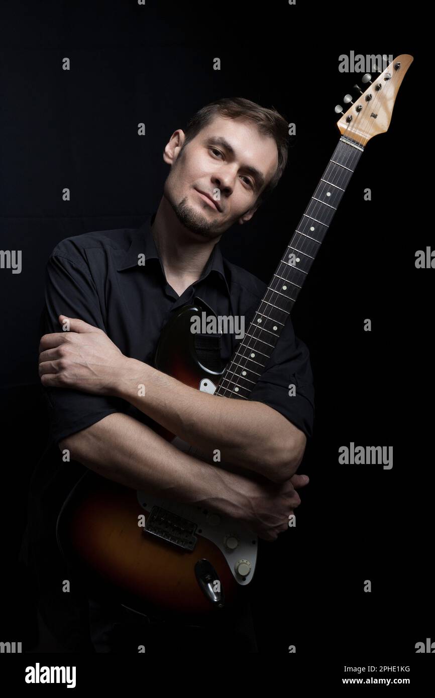 Young man low key portrait hugging electric guitar look at camera on ...