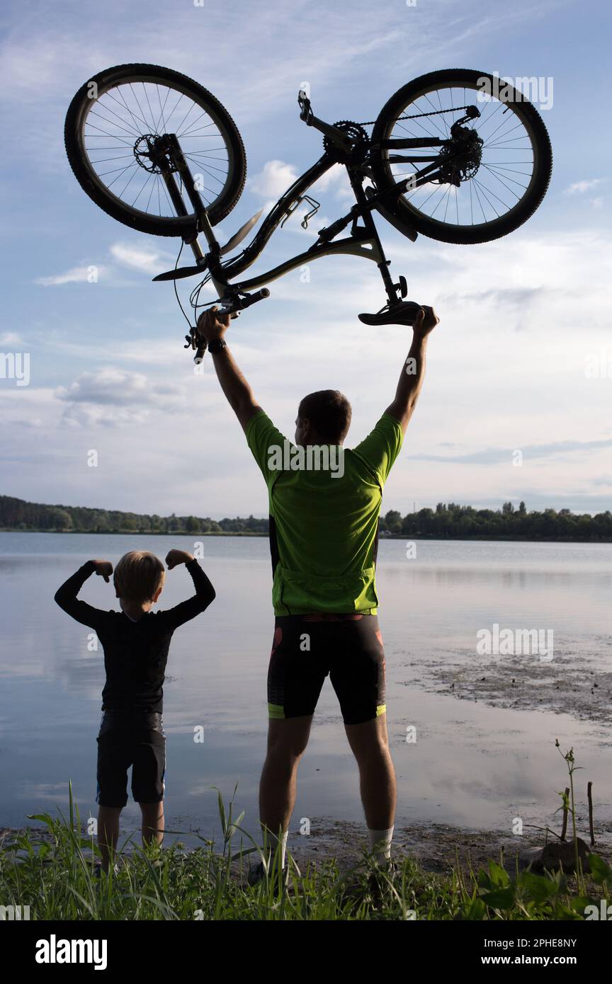 silhouette of adult man raised bicycle above his head. Nearby, boy depicts strong man with hands ...