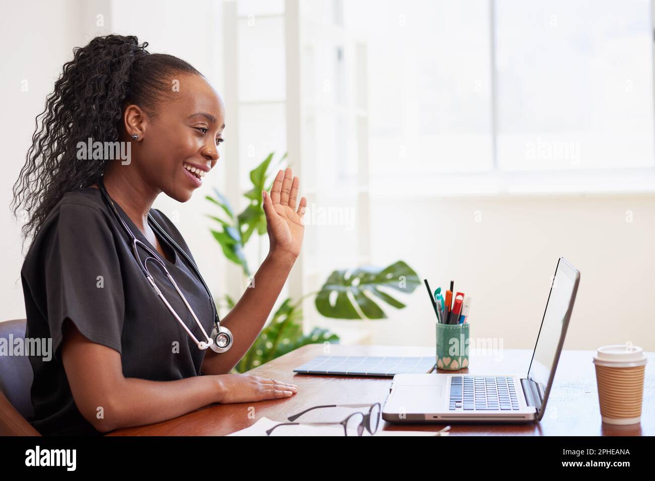 Young Black female doctor waves at patient on conference call ...