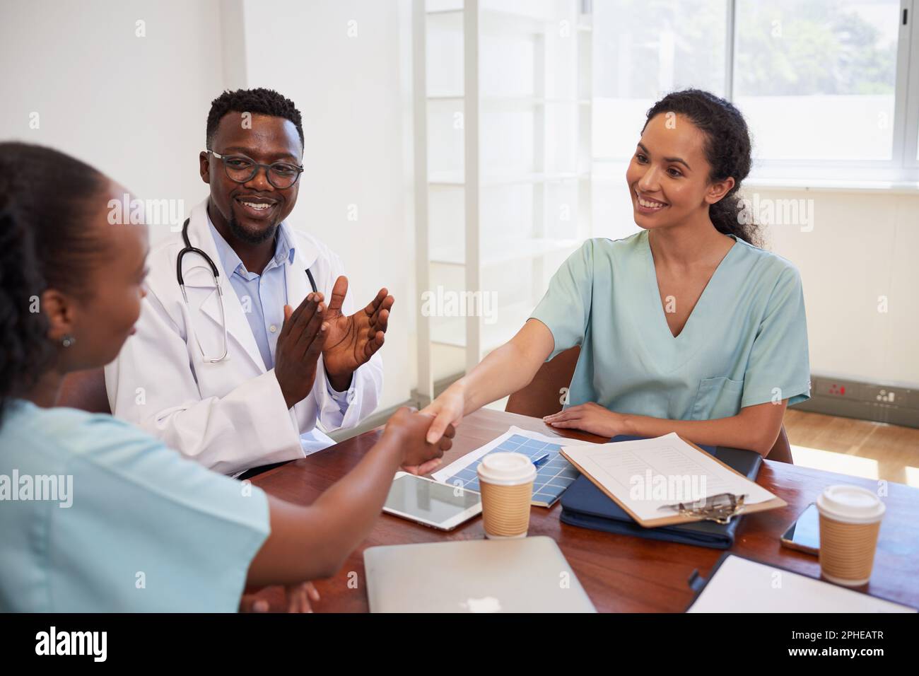 Two doctors shake hands while colleague claps, medical promotion ...