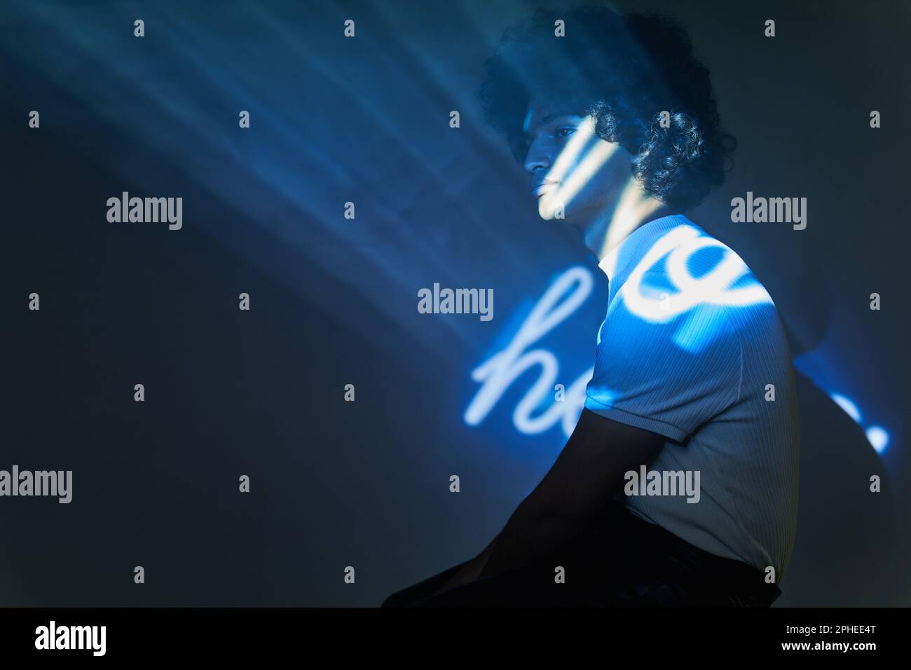 Side view of young Hispanic guy in white t shirt sitting in darkness ...