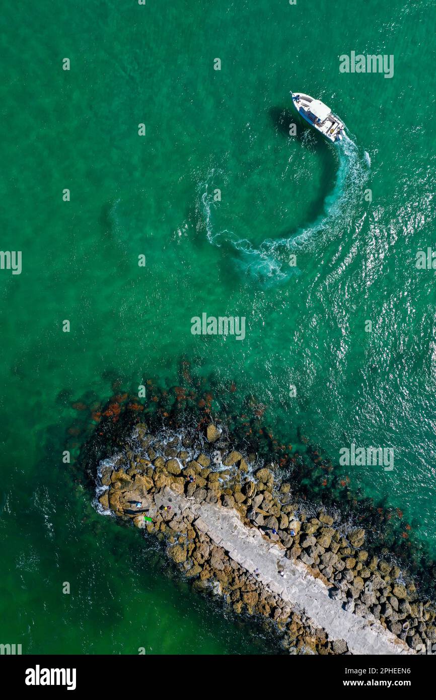 An aerial top-down view of a white boat sailing on bright emerald green ...