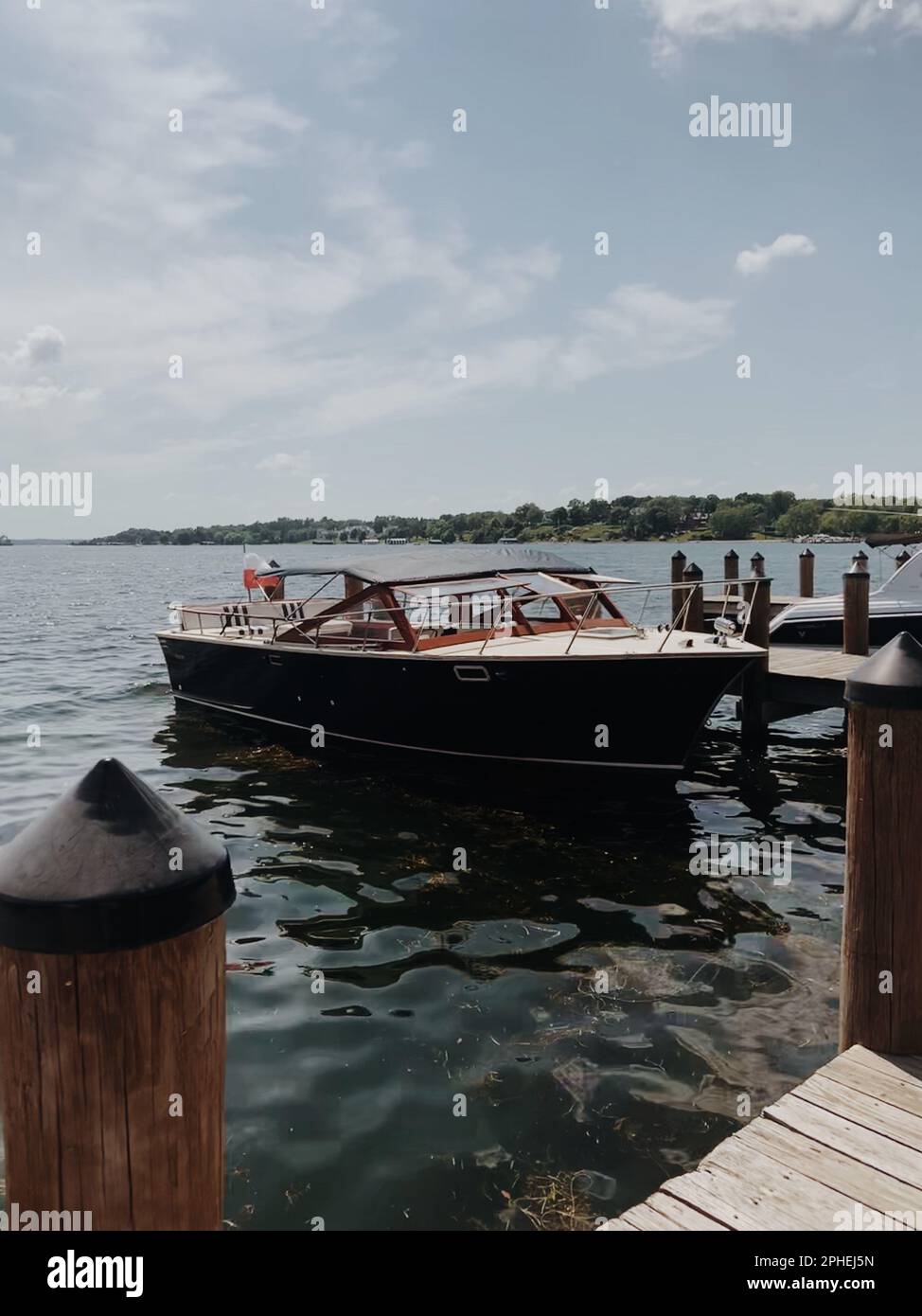 A scenic sunlit wooden dock with a sailing boat docked, gently bobbing ...