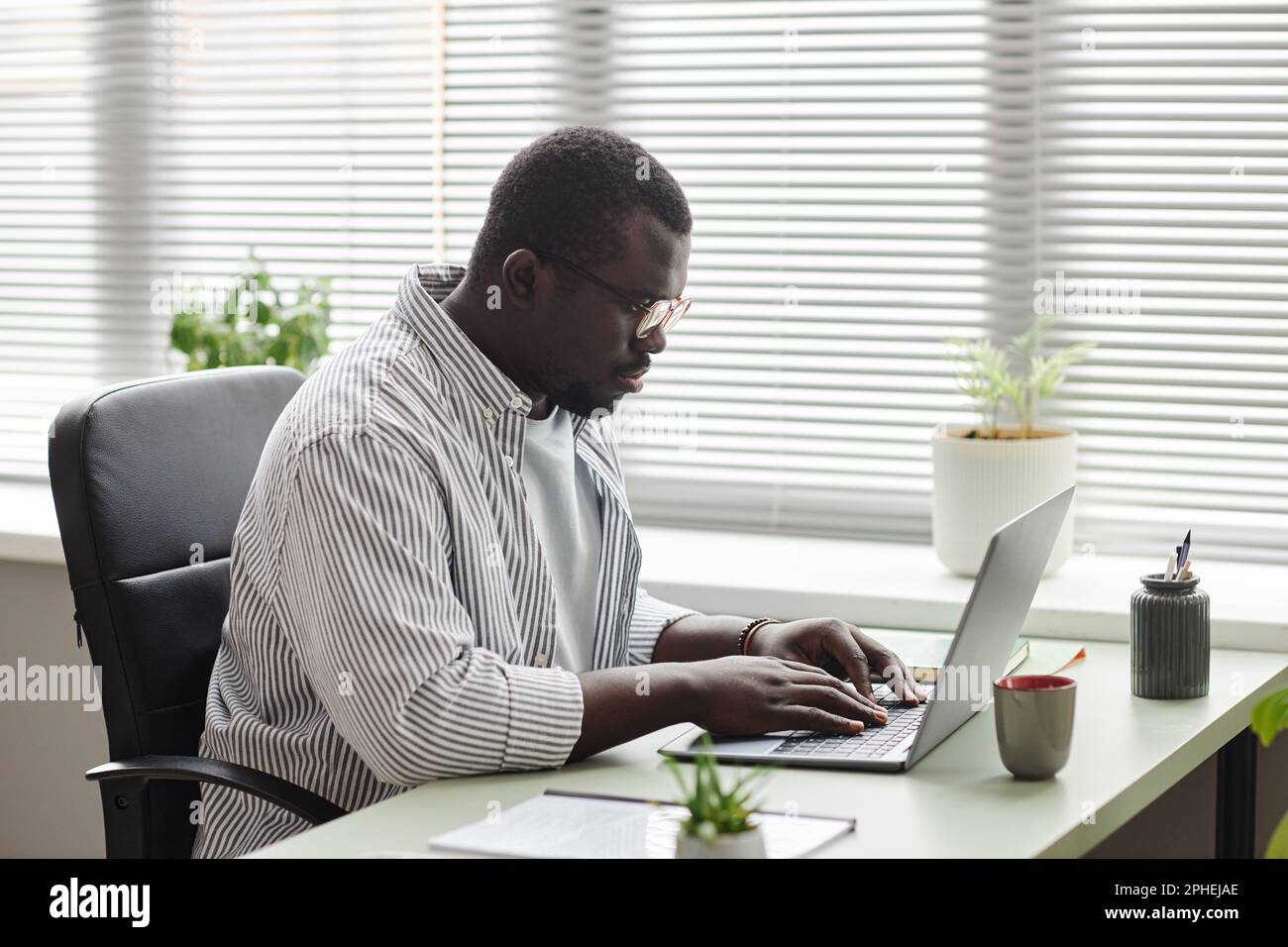 Side view portrait of black businessman typing at laptop keyboard while ...