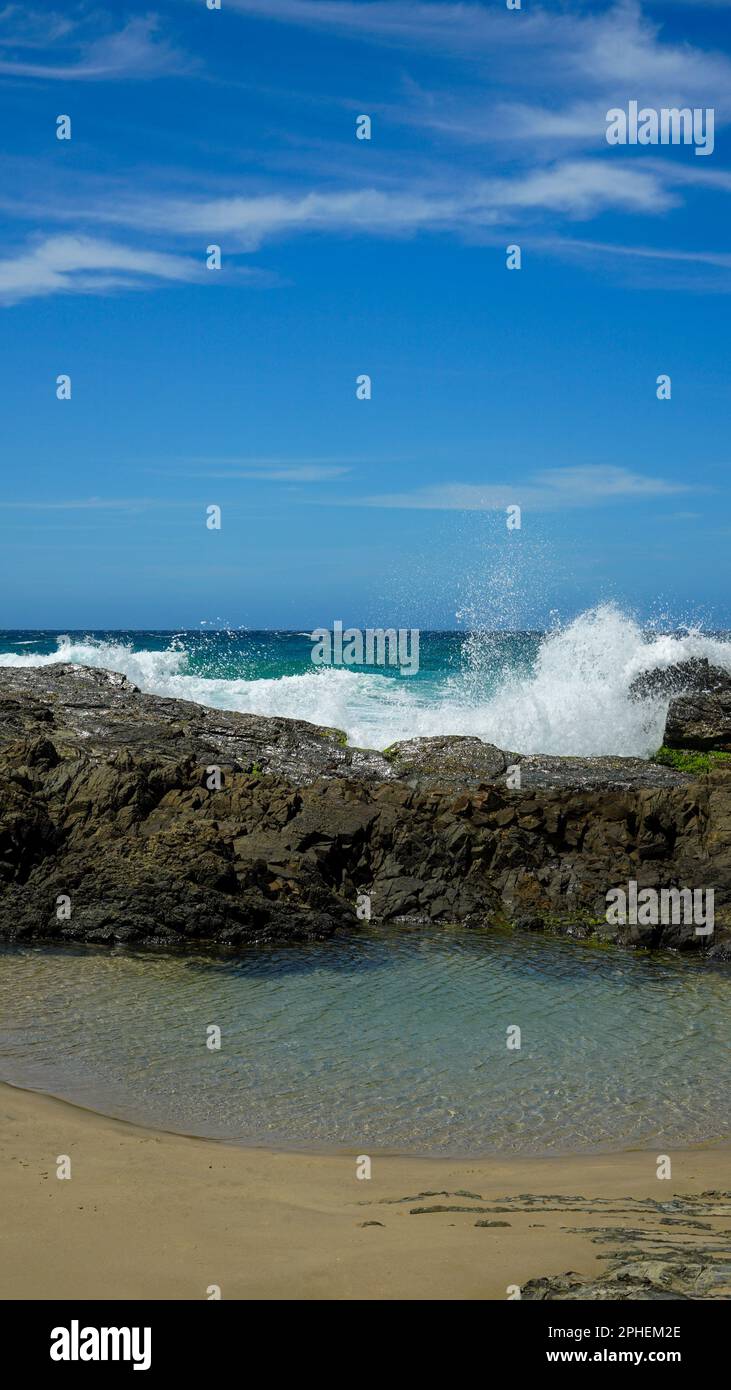 View over a shallow sand-bottomed pool to waves splashing on rocks, and ...