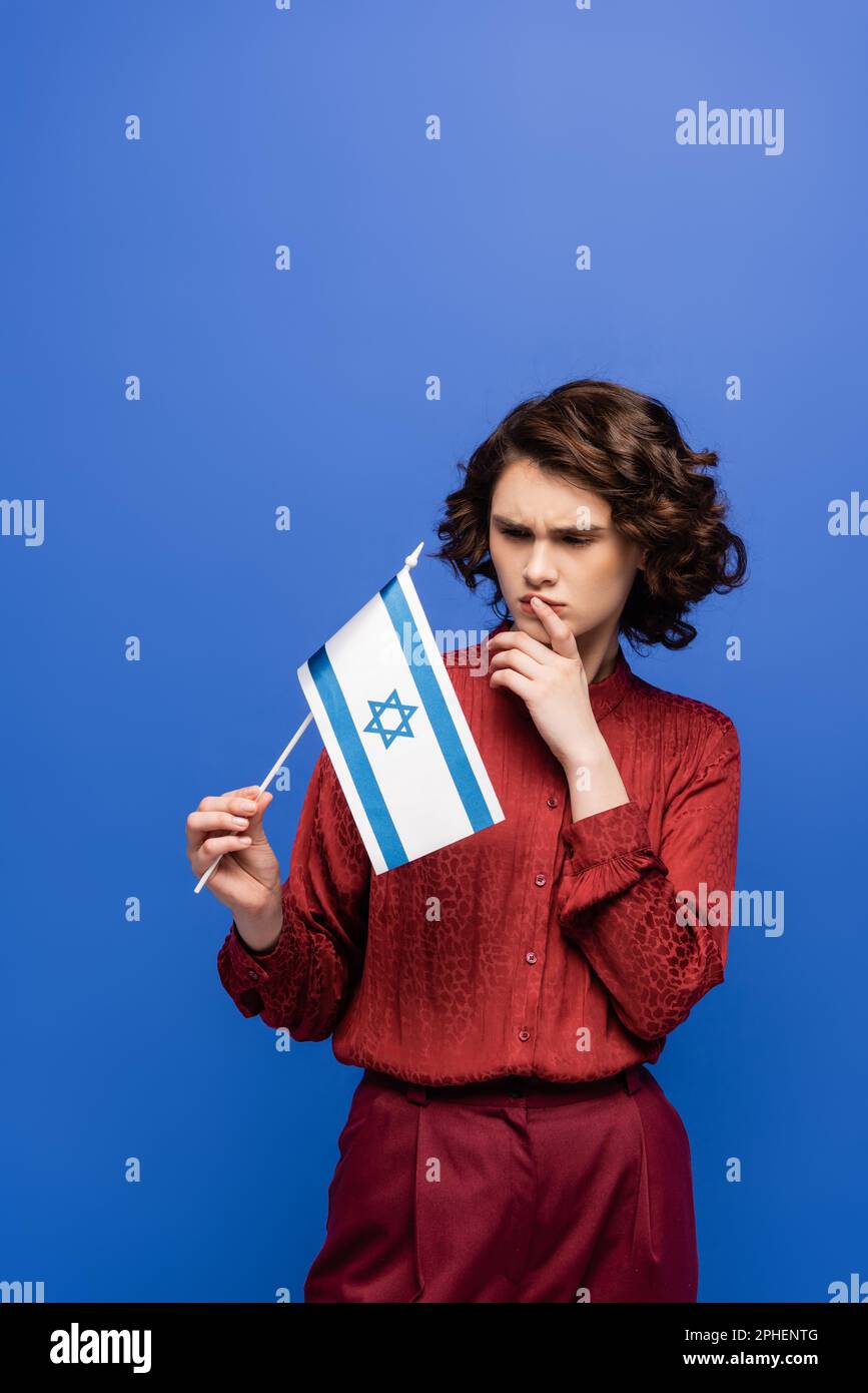 pensive woman with curly hair holding flag of Israel isolated on blue ...