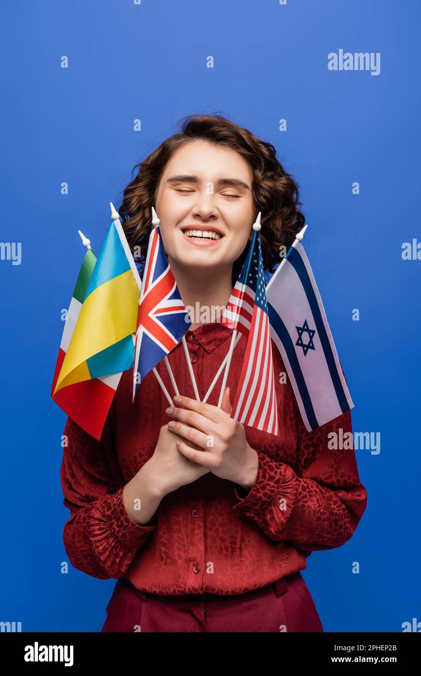 happy young woman holding international flags and smiling with closed ...
