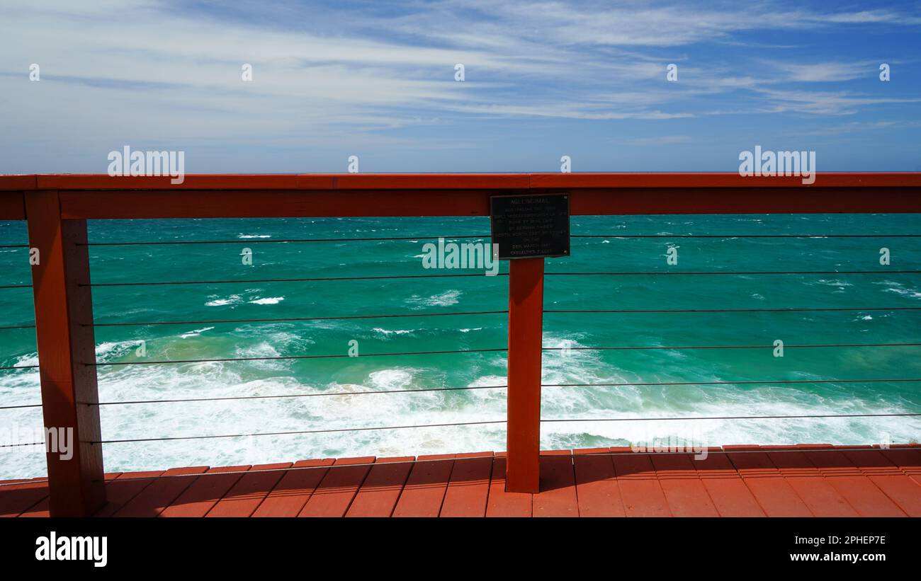 View through a fence to the ocean. Red top rail of the fence is level ...