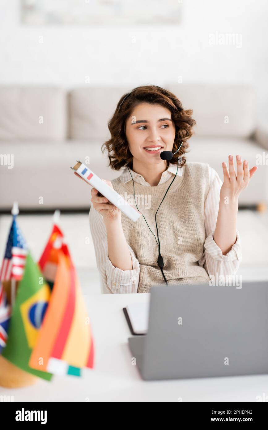 happy language teacher in headset holding French dictionary while ...