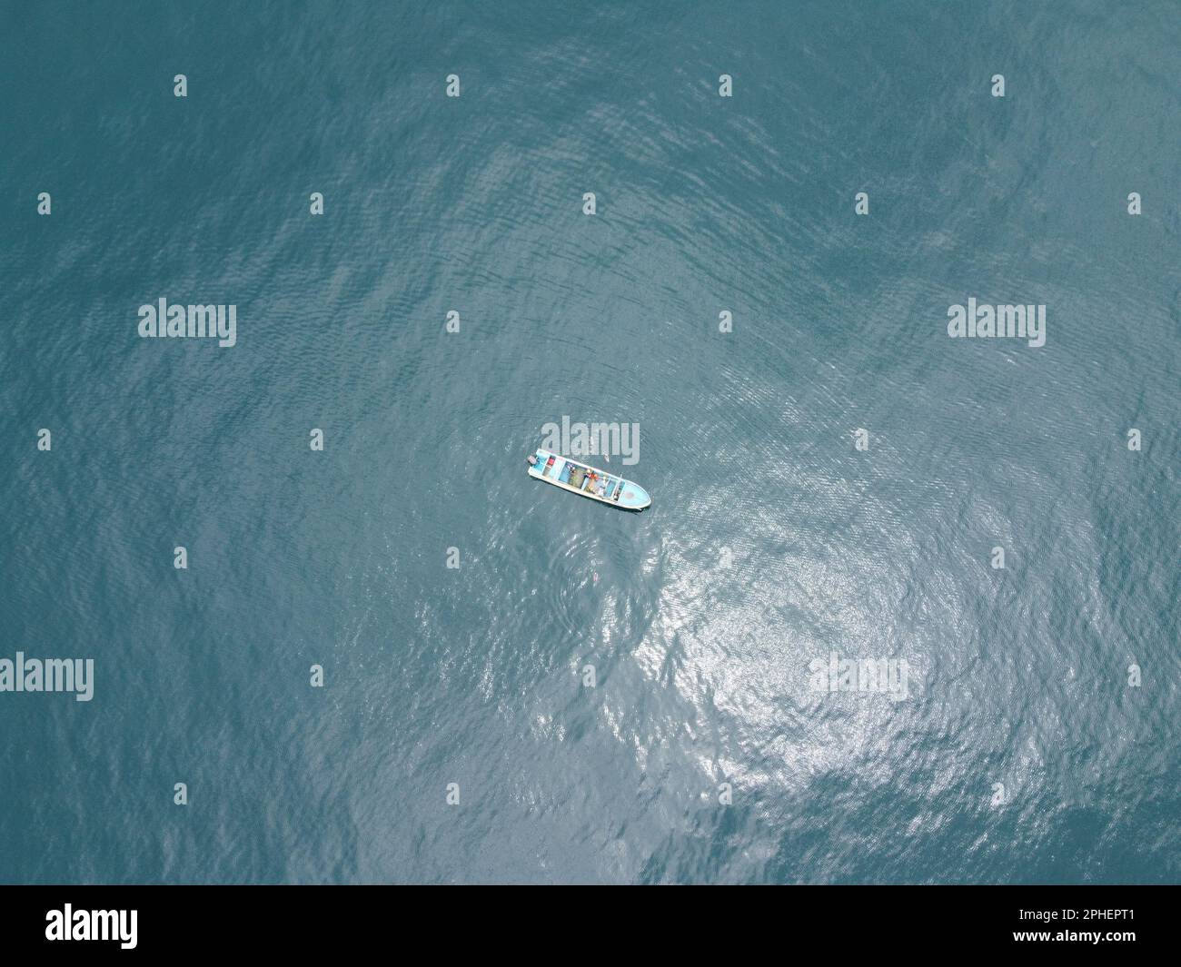 An aerial top view of a boat floating on a pristine blue body of water ...