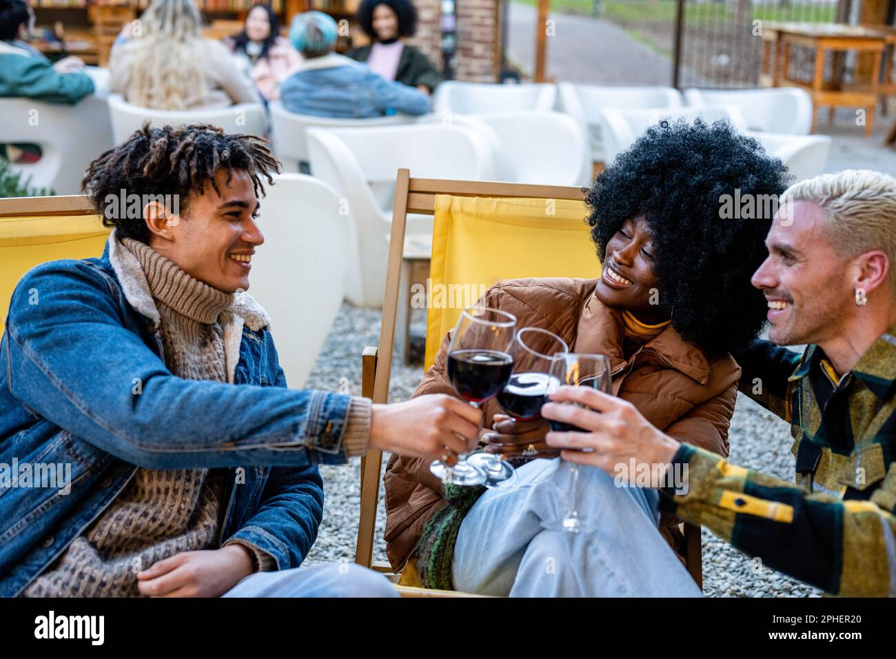 Three friends sitting on deck chairs toasting together with glasses of ...
