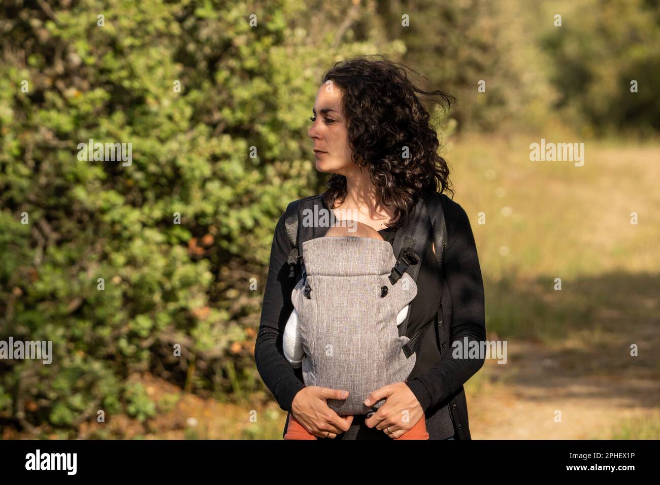 Young mom walking while carrying her newborn baby in an ergonomic ...