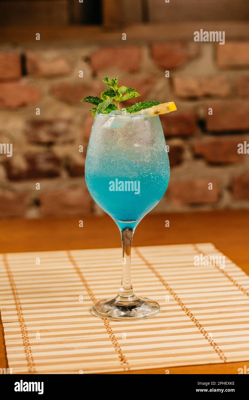 A refreshing blue-colored cocktail with a garnish of citrus and a sprig ...