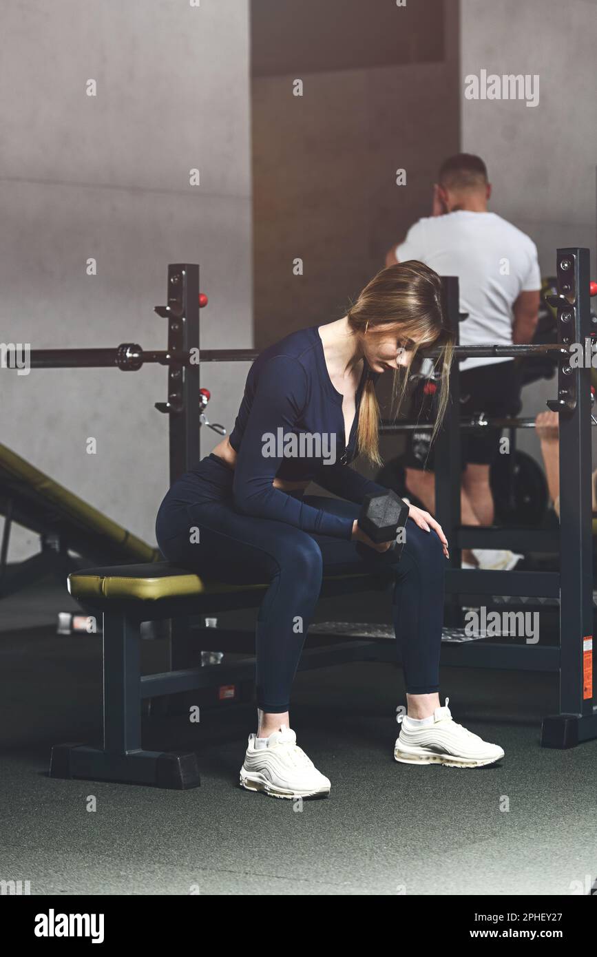 Woman doing biceps curl with dumbbells in seated position. wearing blue ...