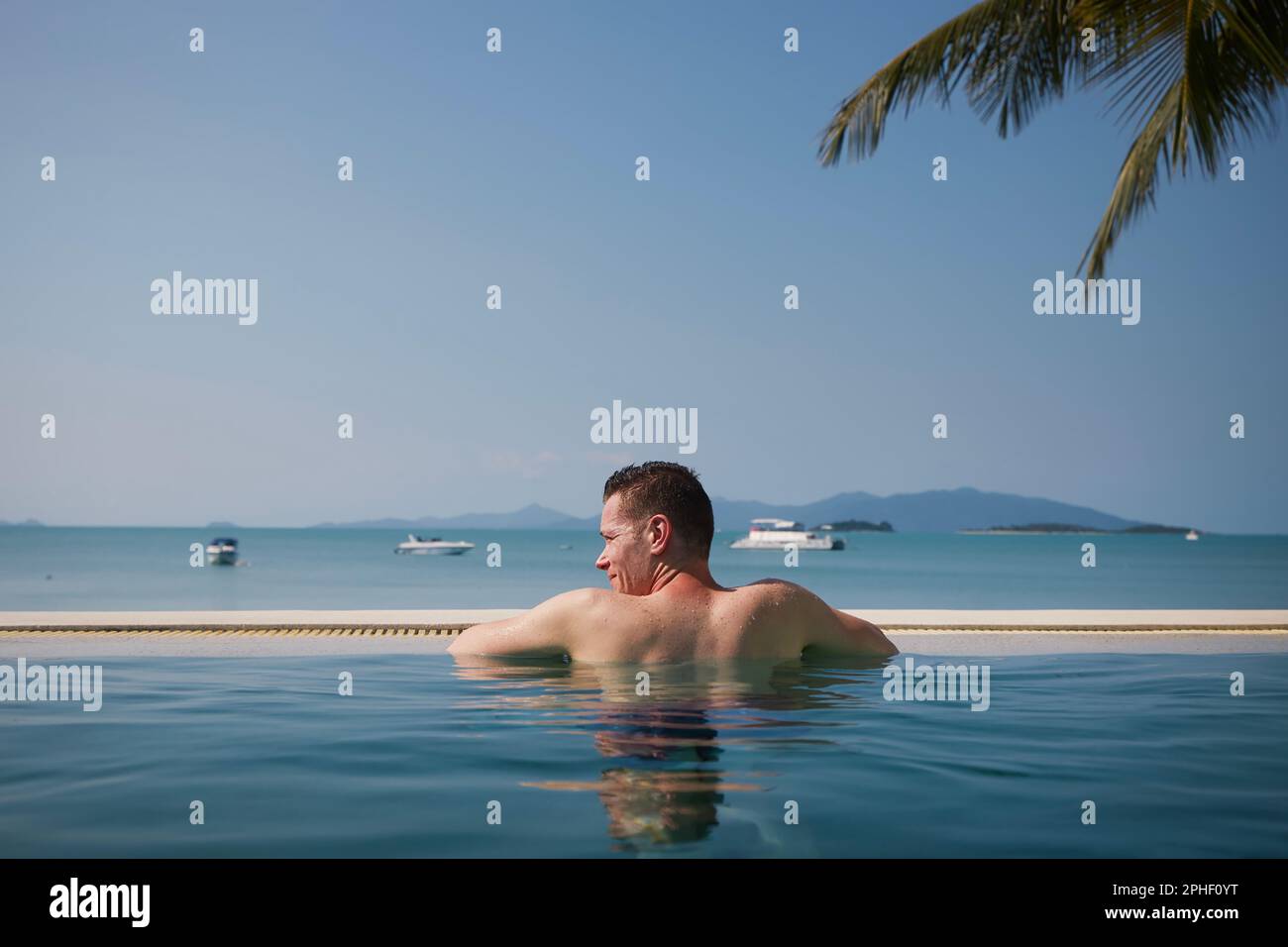 Rear view man while relaxing in swimming pool against sea with islands ...