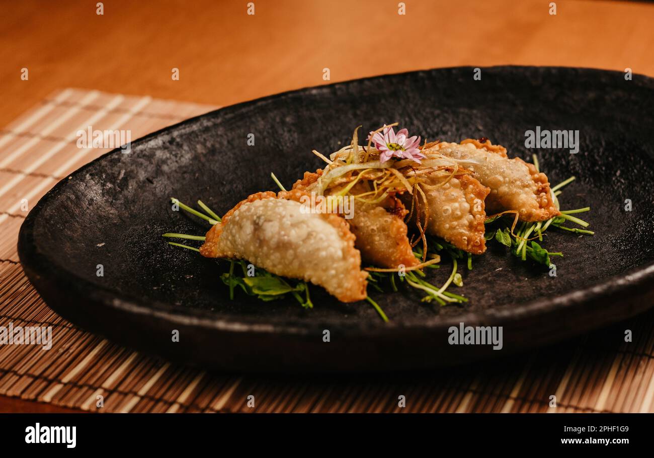 A black plate of food is presented on a wooden table, creating a ...